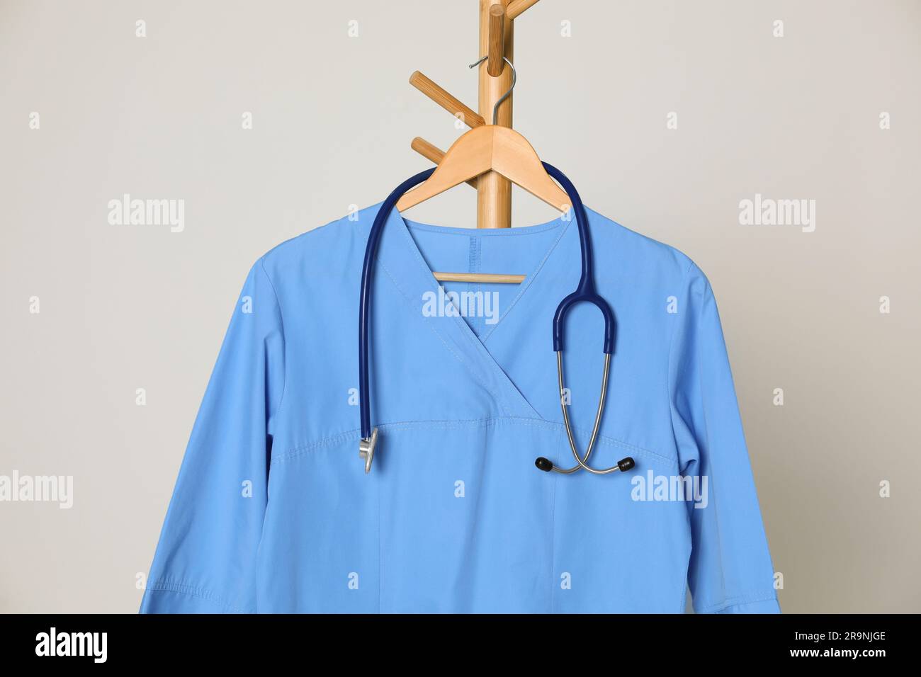 Medical uniform and stethoscope hanging on rack against light grey ...
