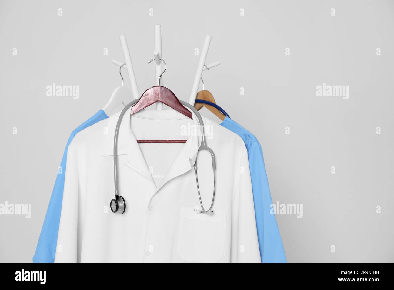 Medical uniforms and stethoscope hanging on rack against light grey ...
