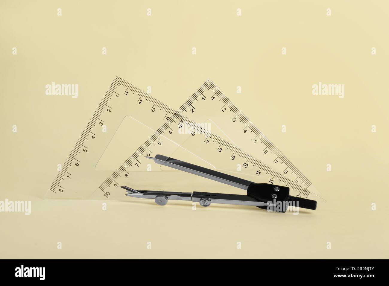 Triangle rulers and compass on light yellow background Stock Photo - Alamy