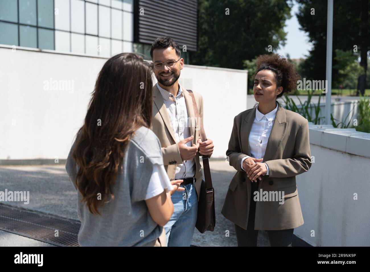 Group of coworkers walking outside in front of office buildings discuss ...