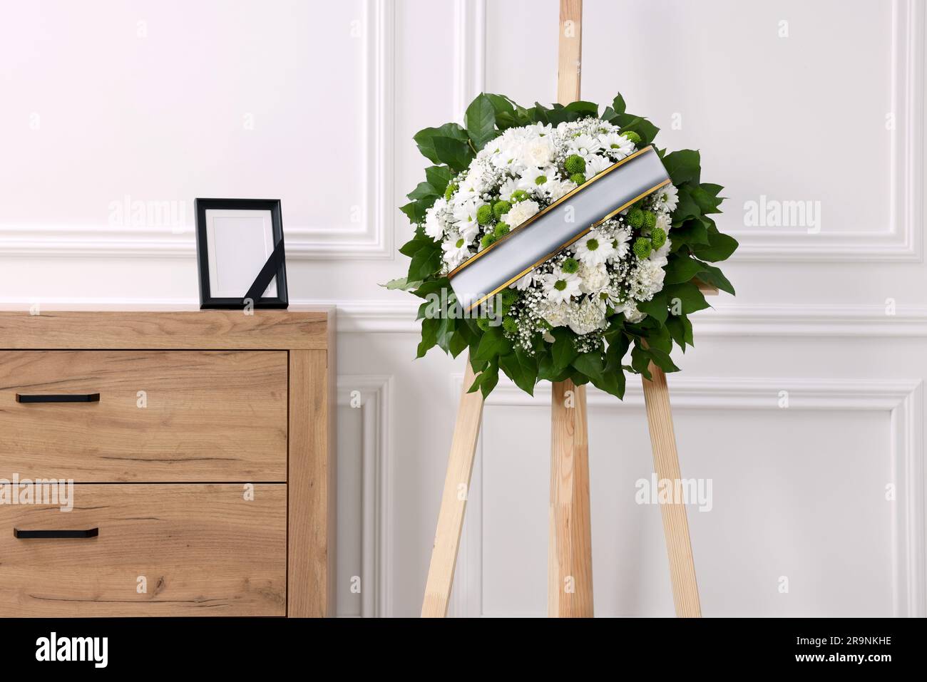 Wreath of flowers and photo frame with black ribbon on commode in room ...