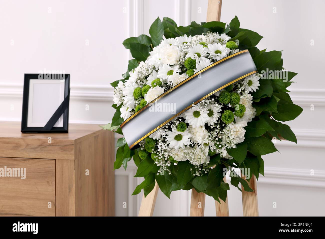 Wreath of flowers and photo frame with black ribbon on commode in room ...