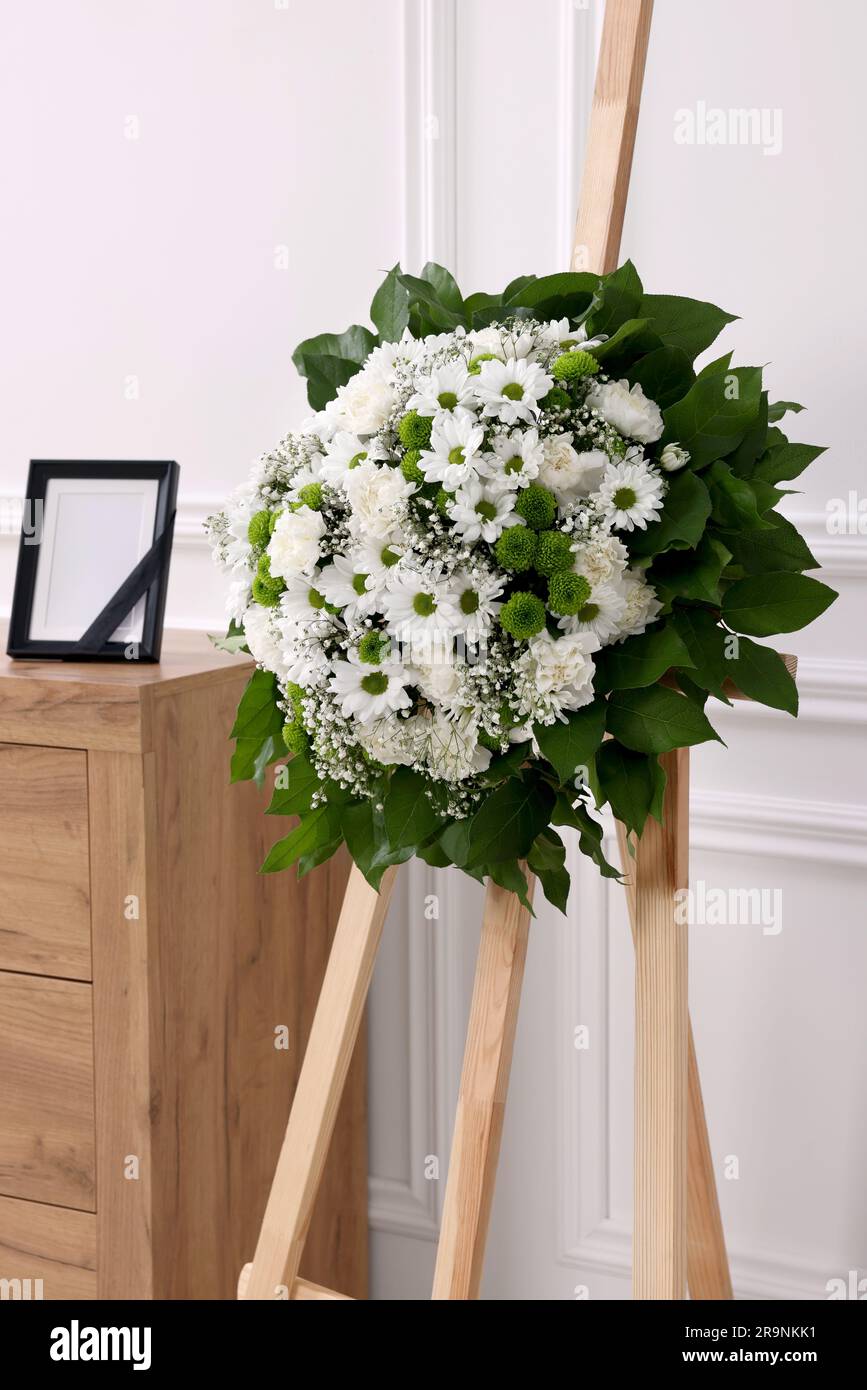 Wreath of flowers and photo frame with black ribbon on commode in room ...