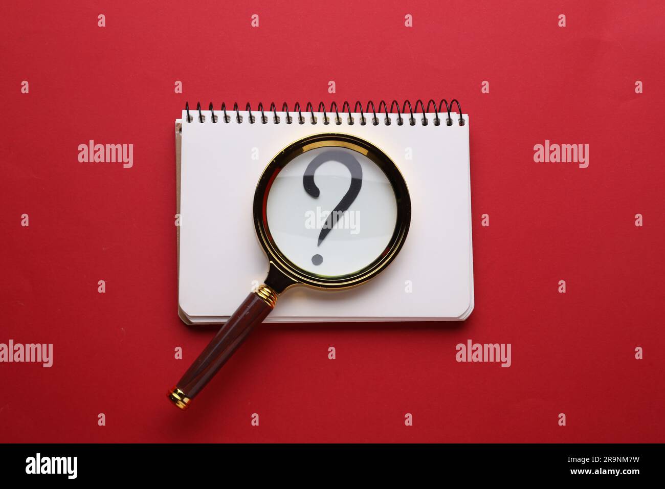 Magnifying glass over notebook with question mark on red background ...