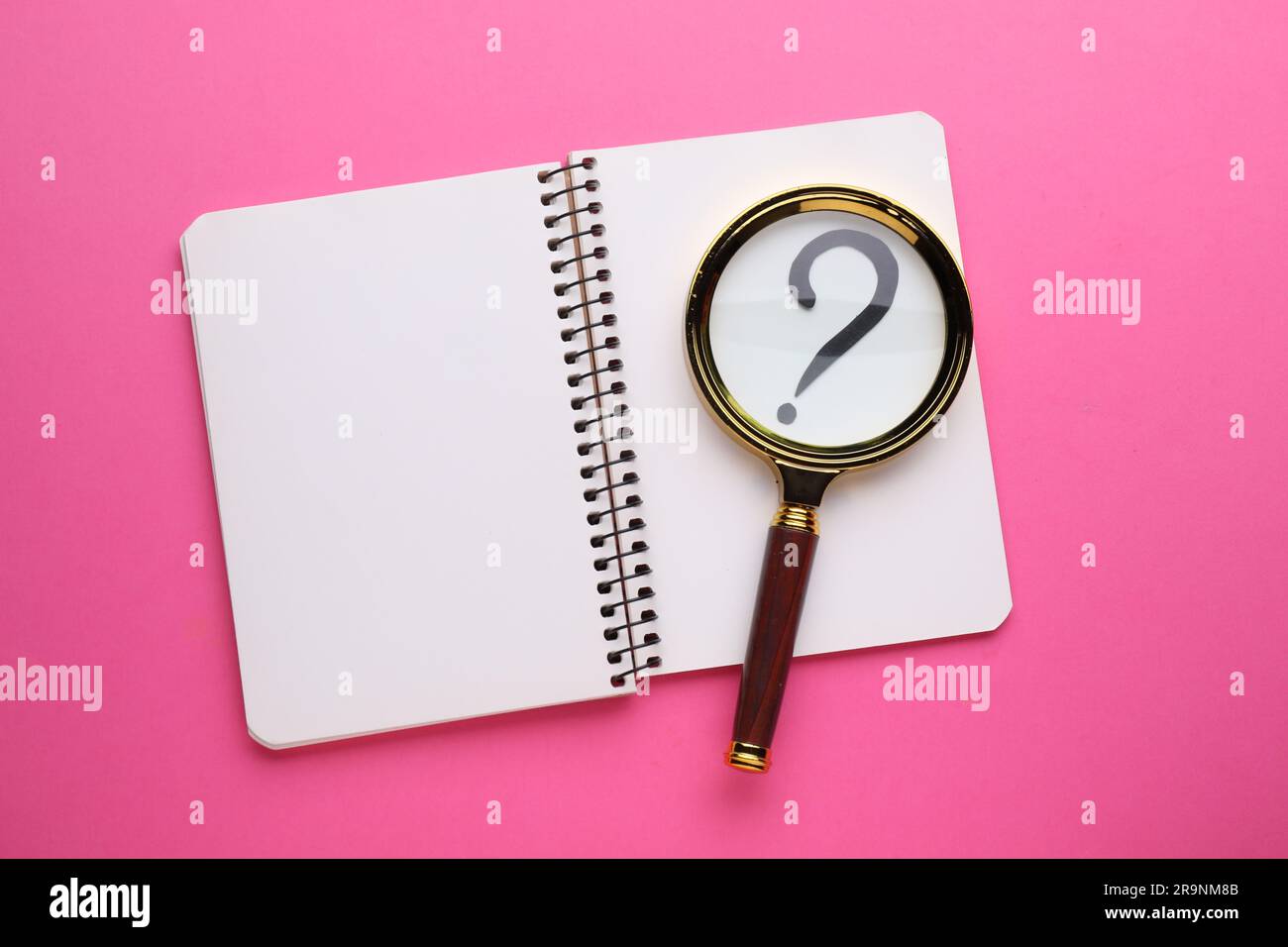 Magnifying glass over notebook with question mark on pink background ...