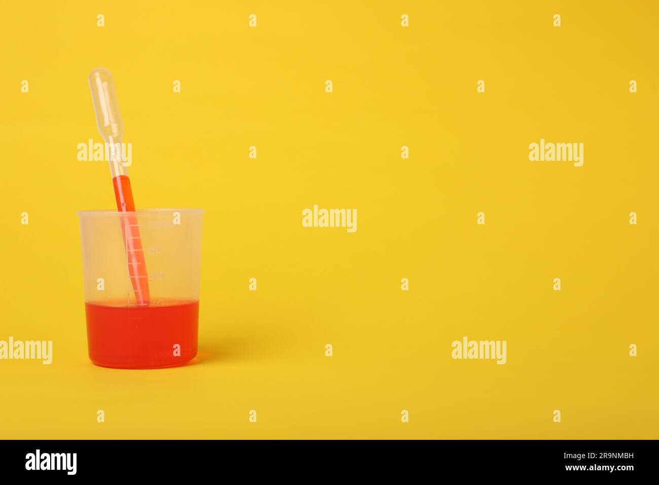 Beaker with liquid and stirring rod on yellow background, space for ...