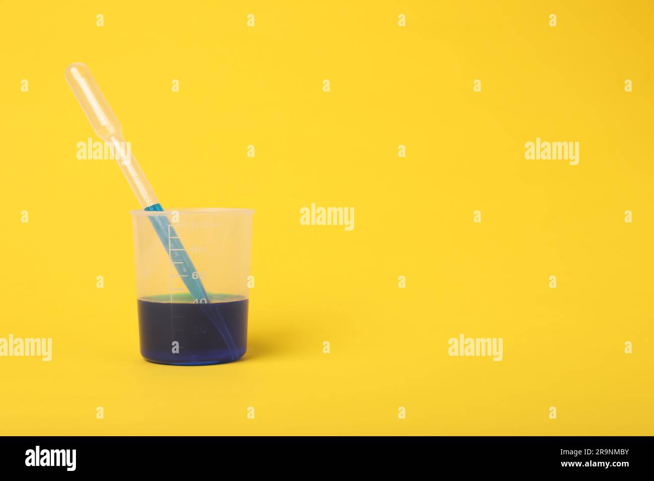 Beaker with liquid and stirring rod on yellow background, space for ...