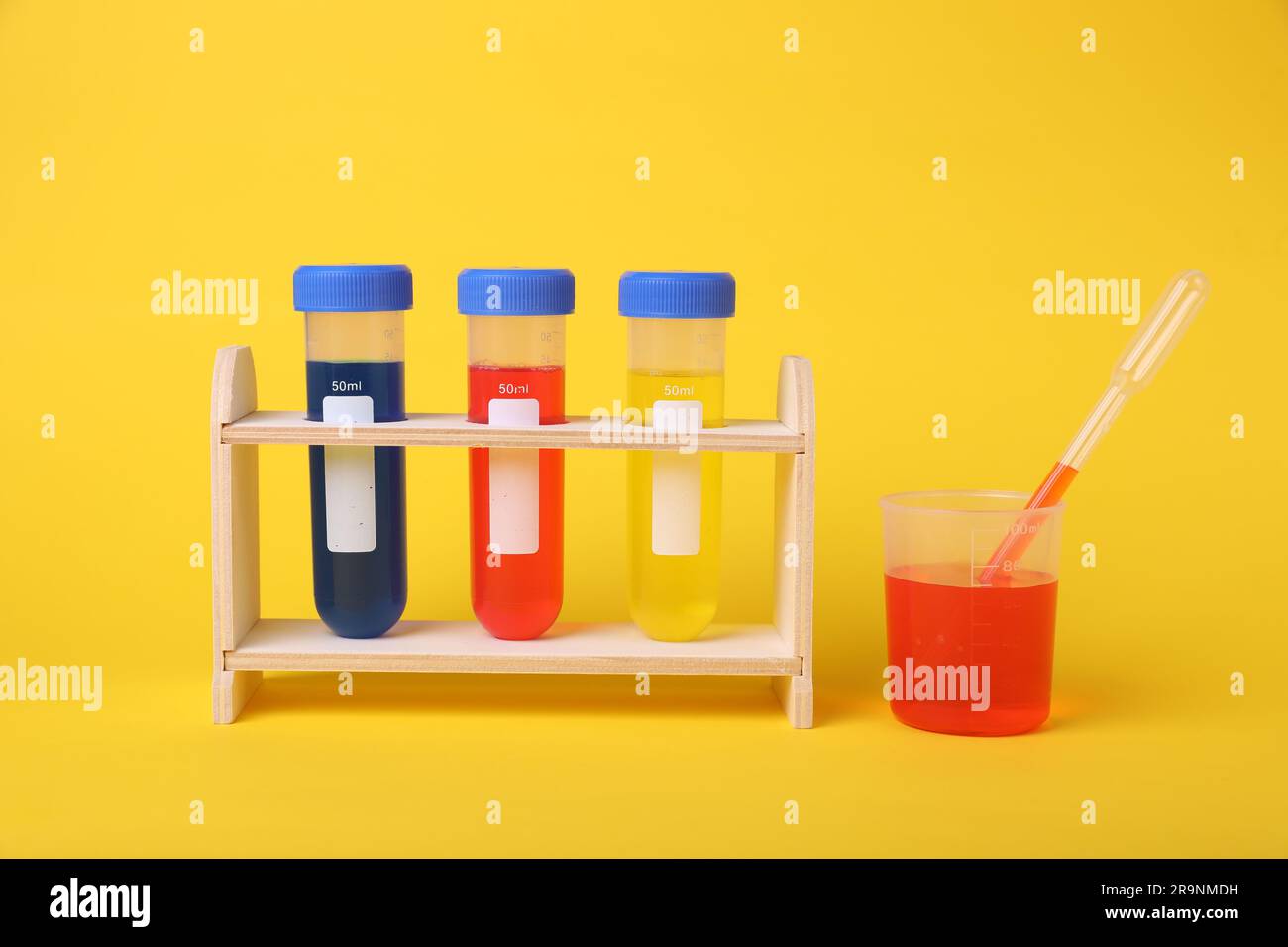 Beaker and test tubes with colorful liquids in wooden stand on yellow ...