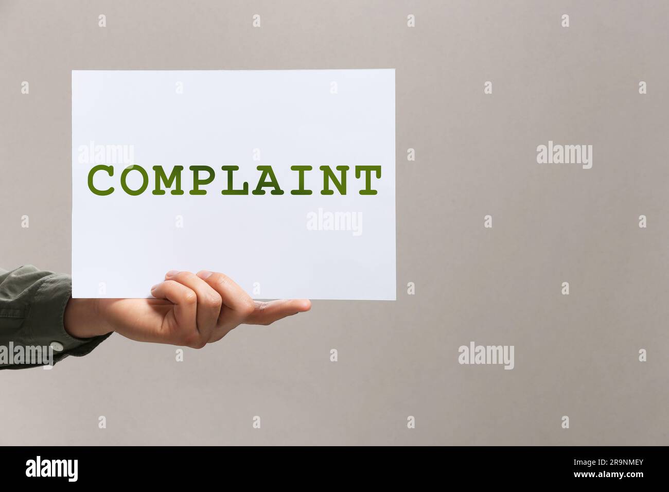 Man holding sheet of paper with word Complaint on grey background ...