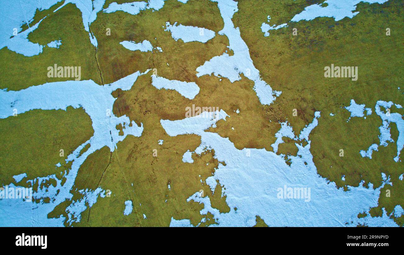 An aerial shot of the green field spotted with white snow Stock Photo ...