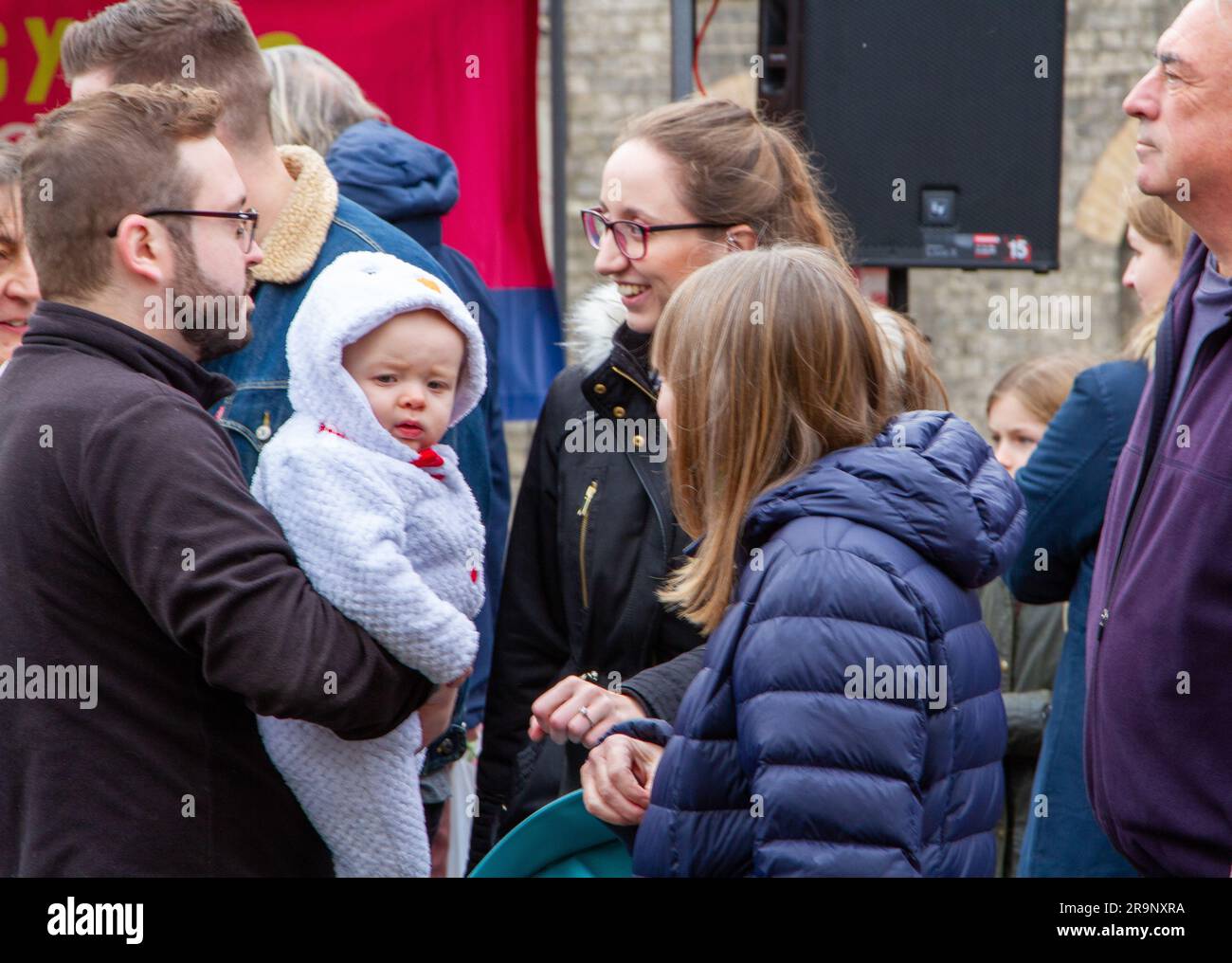 A proud father holds his baby in a pale blue romper suit at a street ...