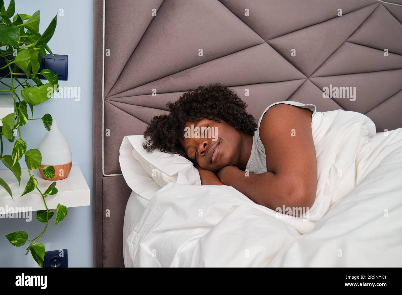 Happy african young woman sleeping on white sheets in bed in a room ...