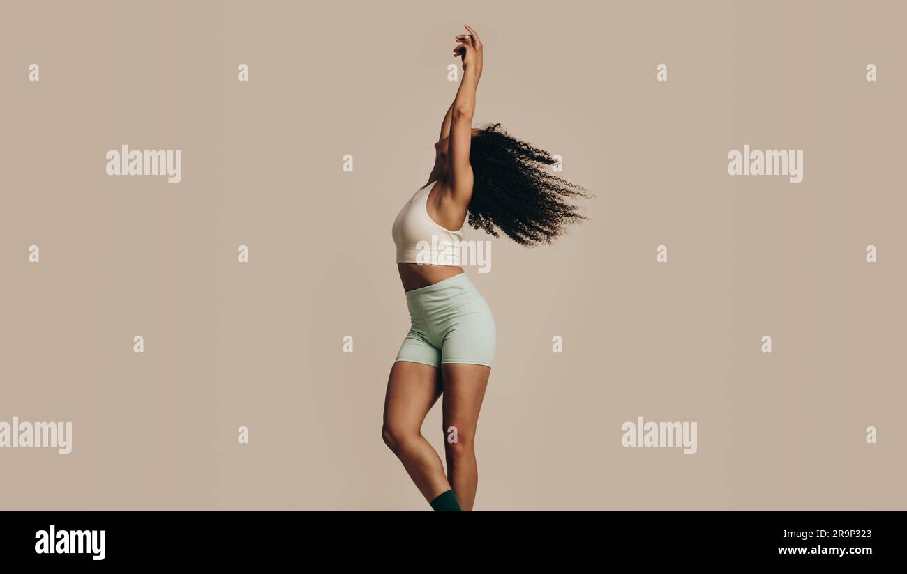 Fit woman standing in a studio in gym wear, moving her body with her ...