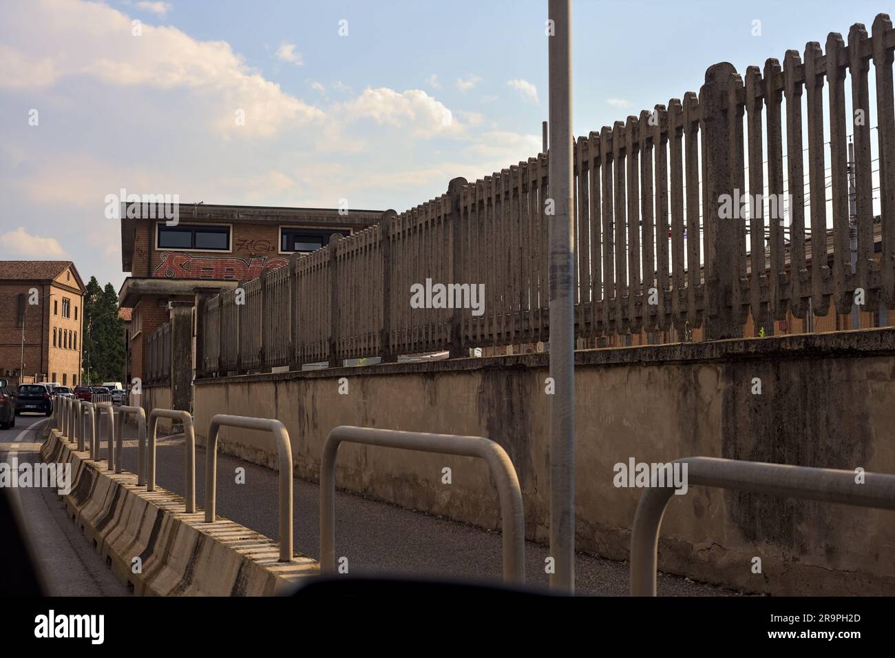Railroad track and over head cables seen from a pavement behind a fence ...