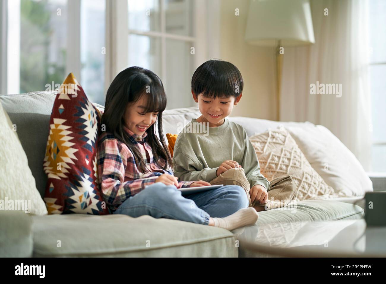 little asian children brother and sister sitting on family couch at ...
