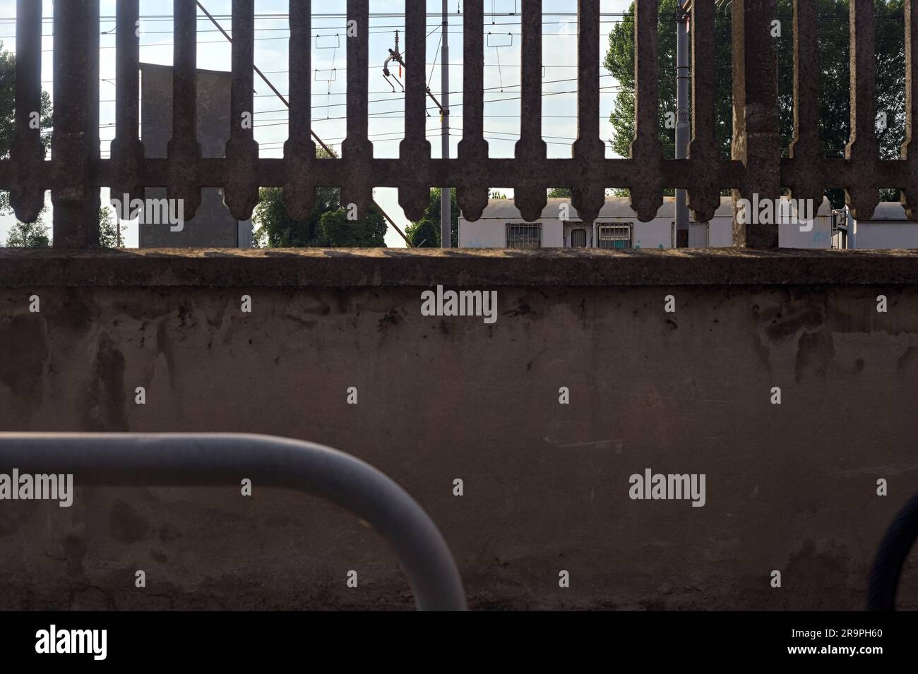 Railroad track and over head cables seen from a pavement behind a fence ...