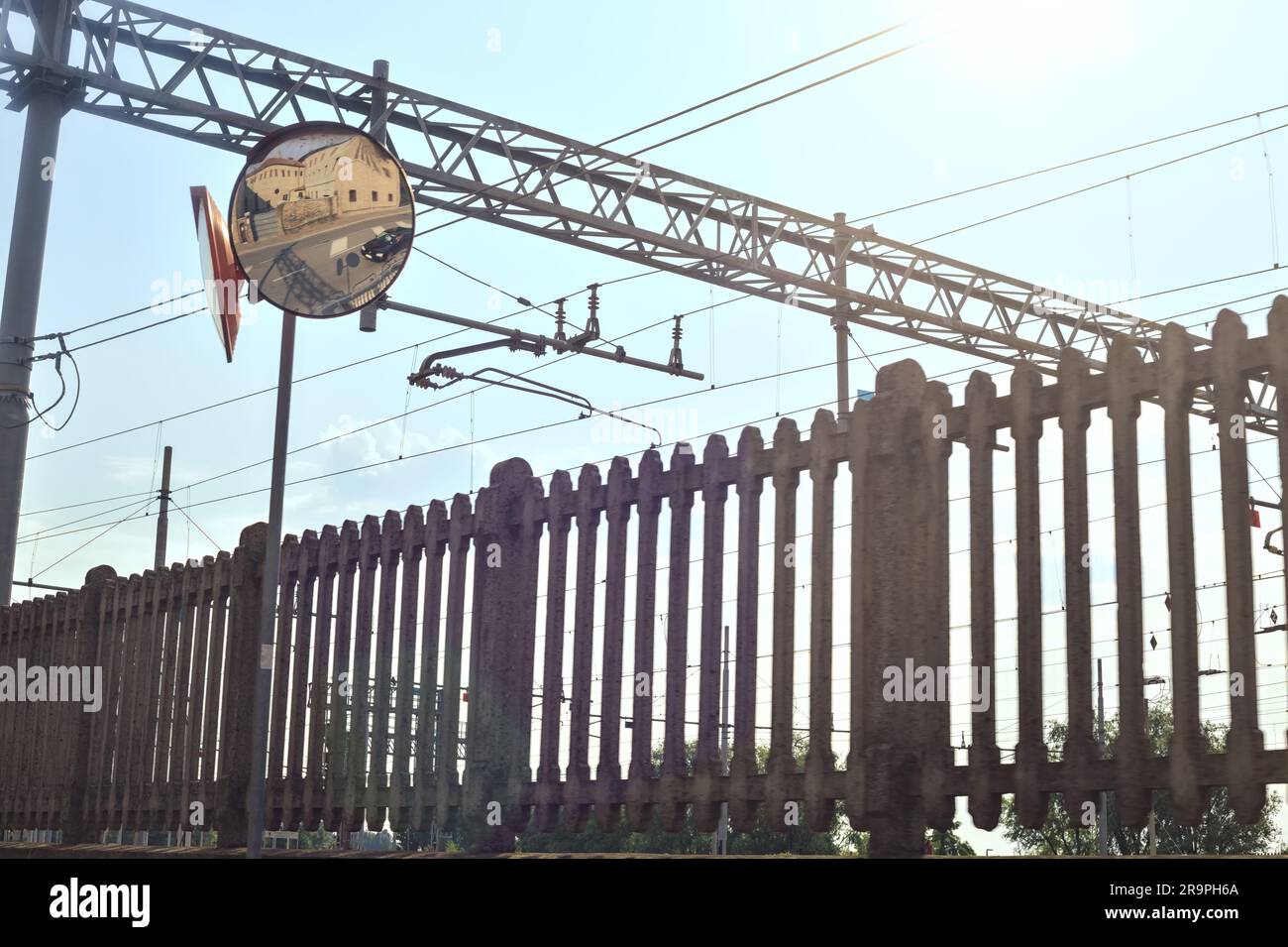 Railroad track and over head cables seen from a pavement behind a fence ...
