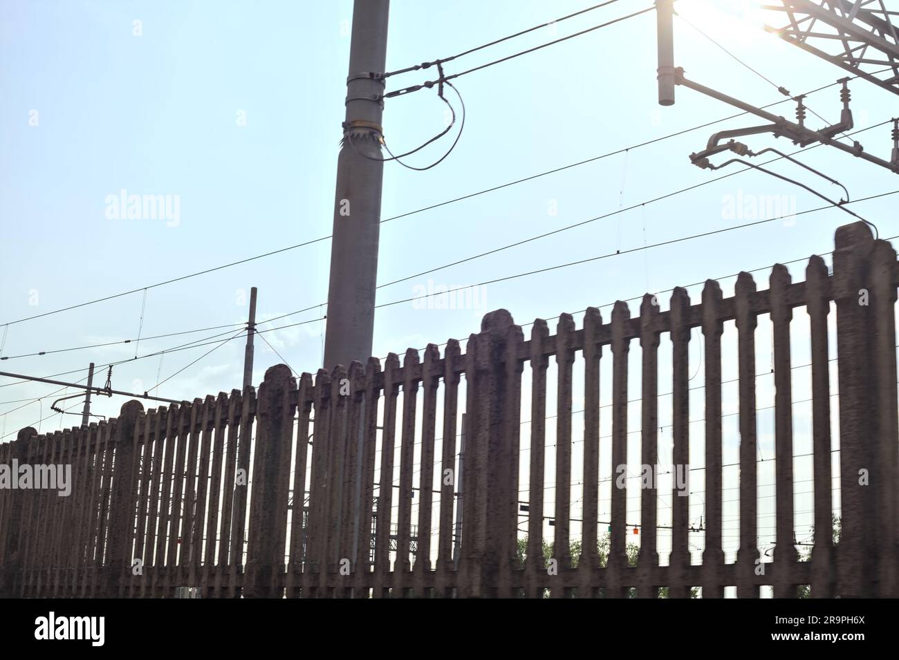 Railroad track and over head cables seen from a pavement behind a fence ...