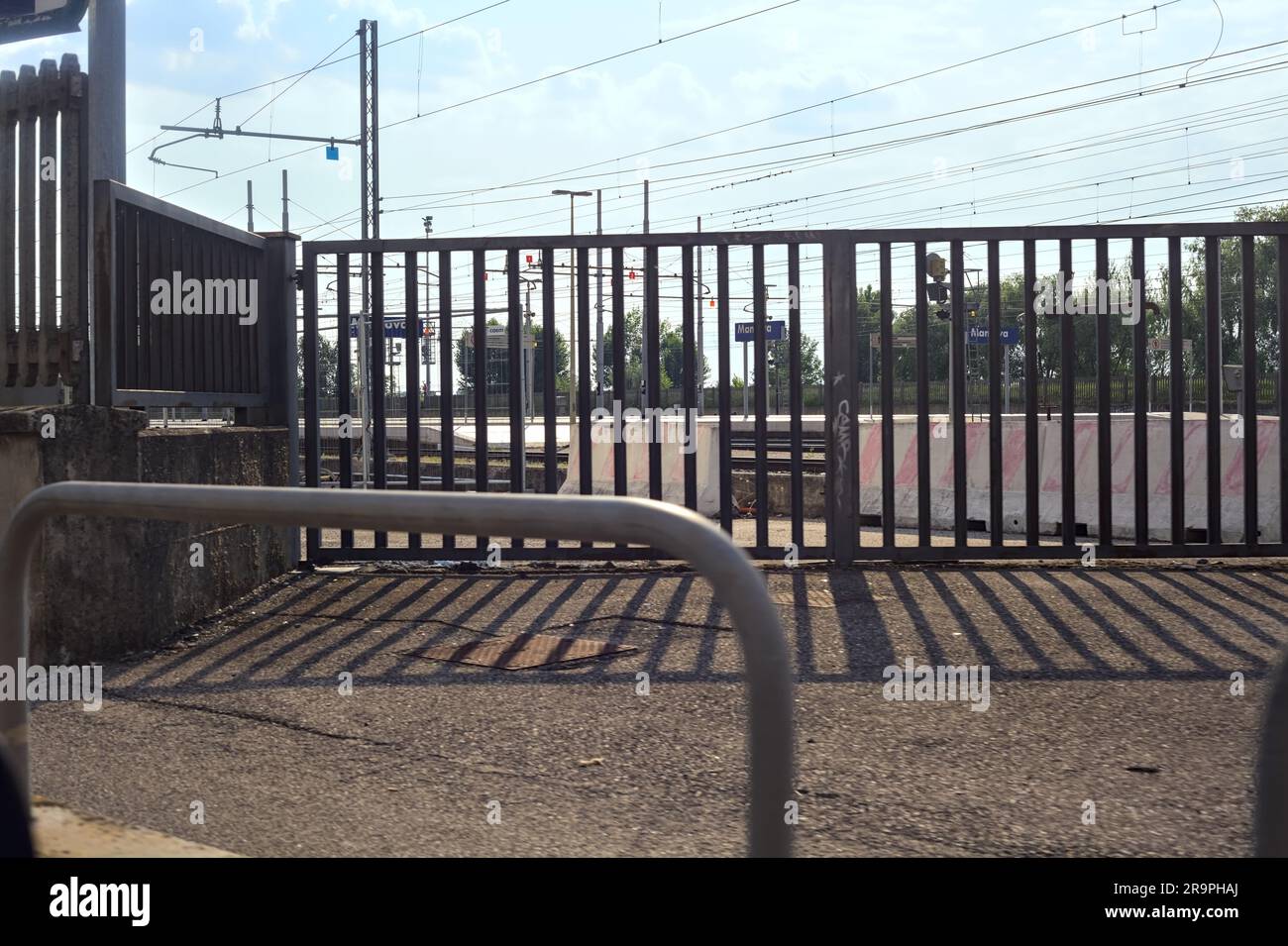 Railroad track and over head cables seen from a pavement behind a fence ...