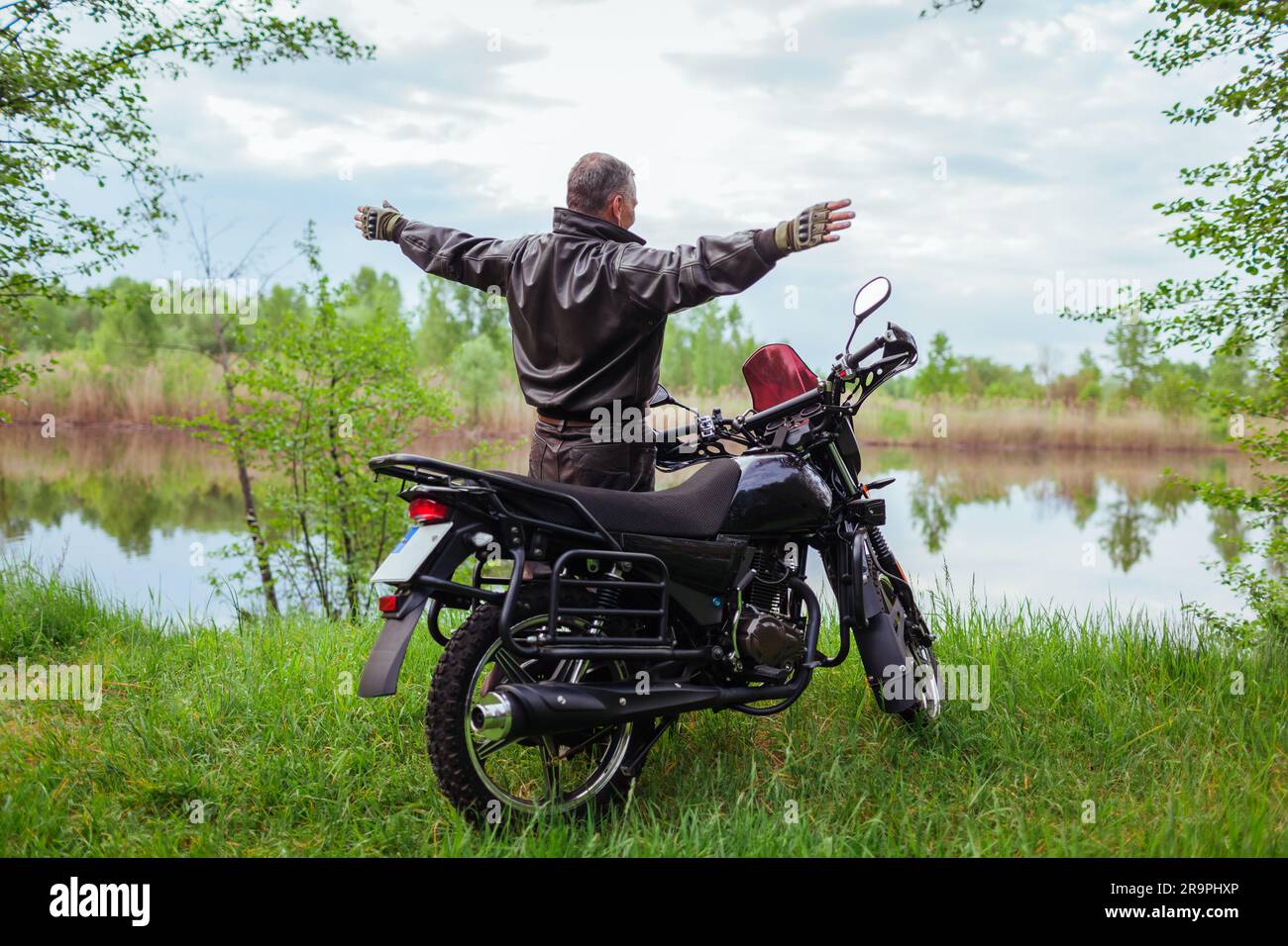 Back view of happy senior biker raising arms enjoying river landscape ...