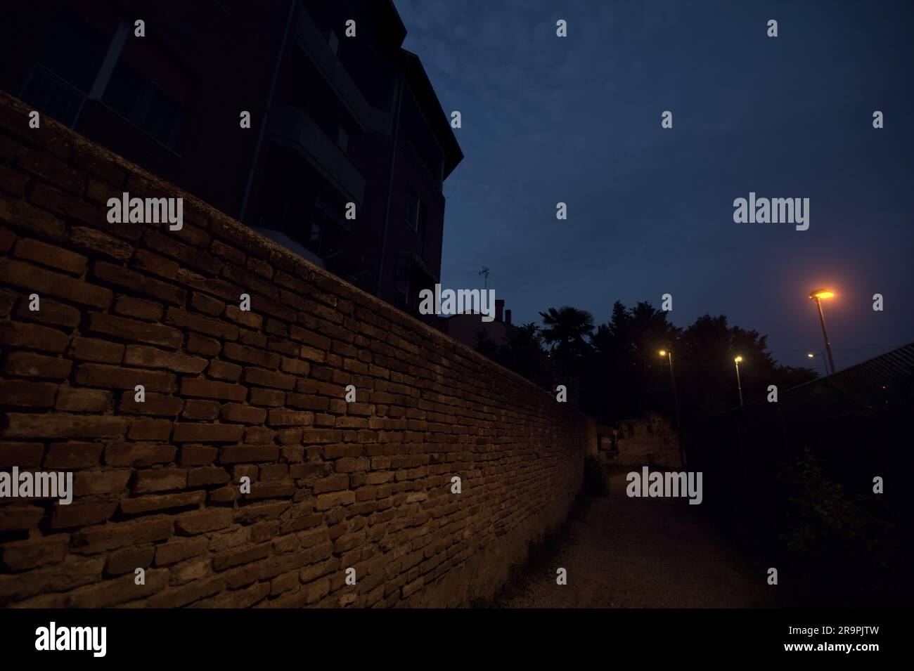 Path bordered by a brick wall and a fence with street lamps in the ...