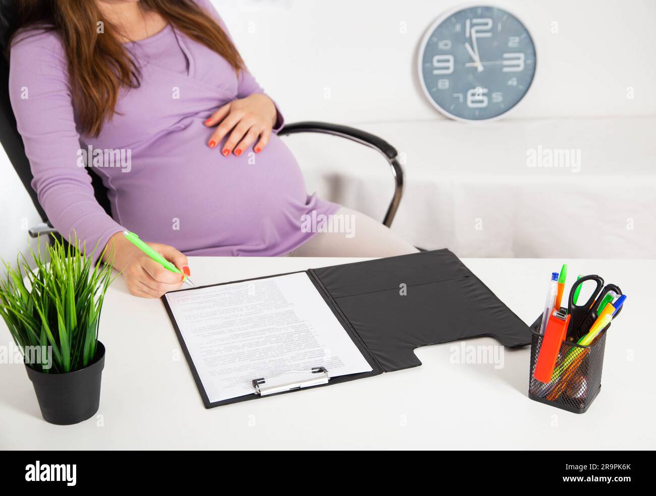 a pregnant girl in the office at work signs documents. The concept of ...