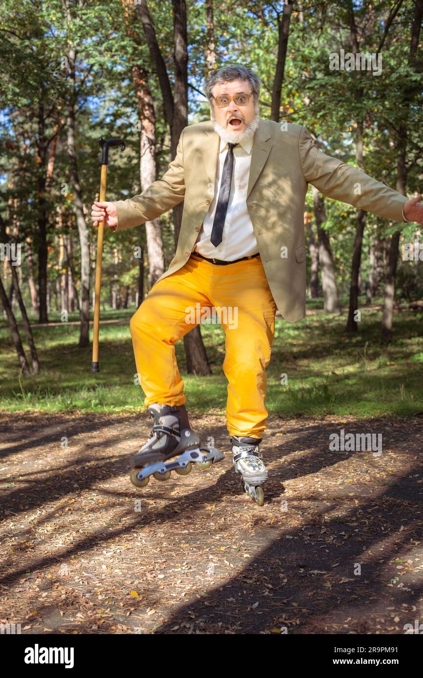 Funny old man is roller skating in the park. An active grandfather with ...