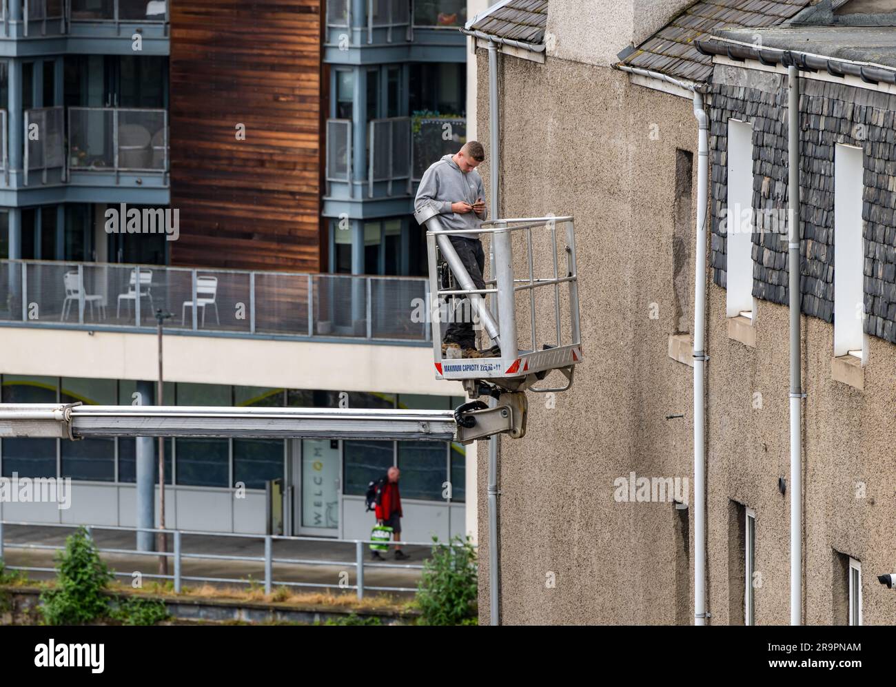 Workman in cherry picker looking at his mobile phone, Leith, Edinburgh ...