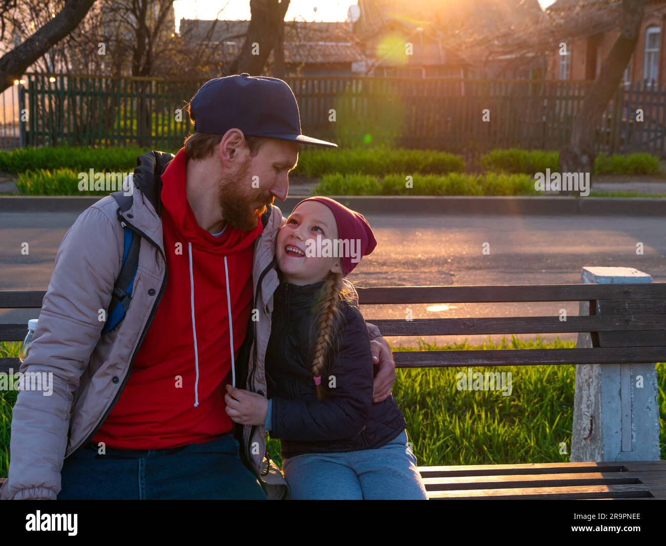 Happy girl with long braided hair and father in spring park sits on a ...
