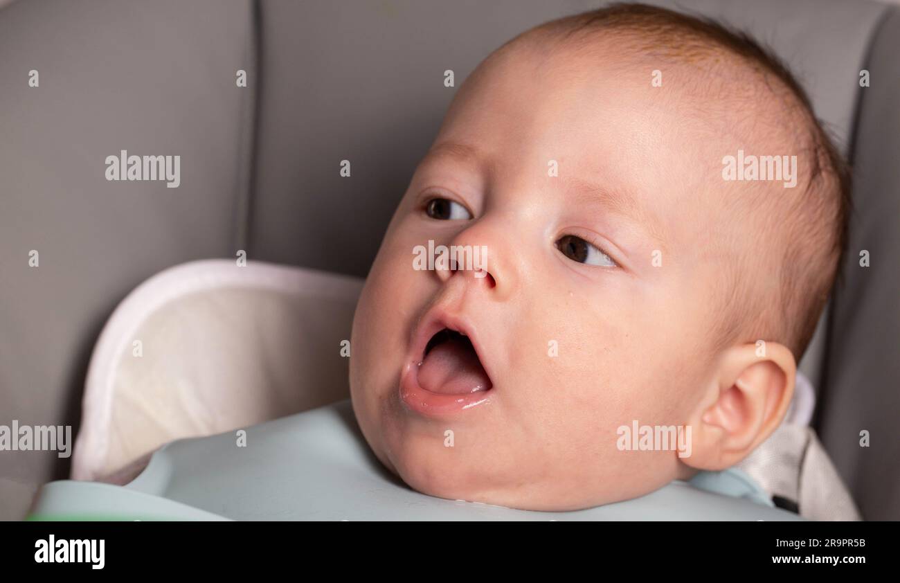 A handsome little boy aged 5 months sits with his mouth open and shows ...
