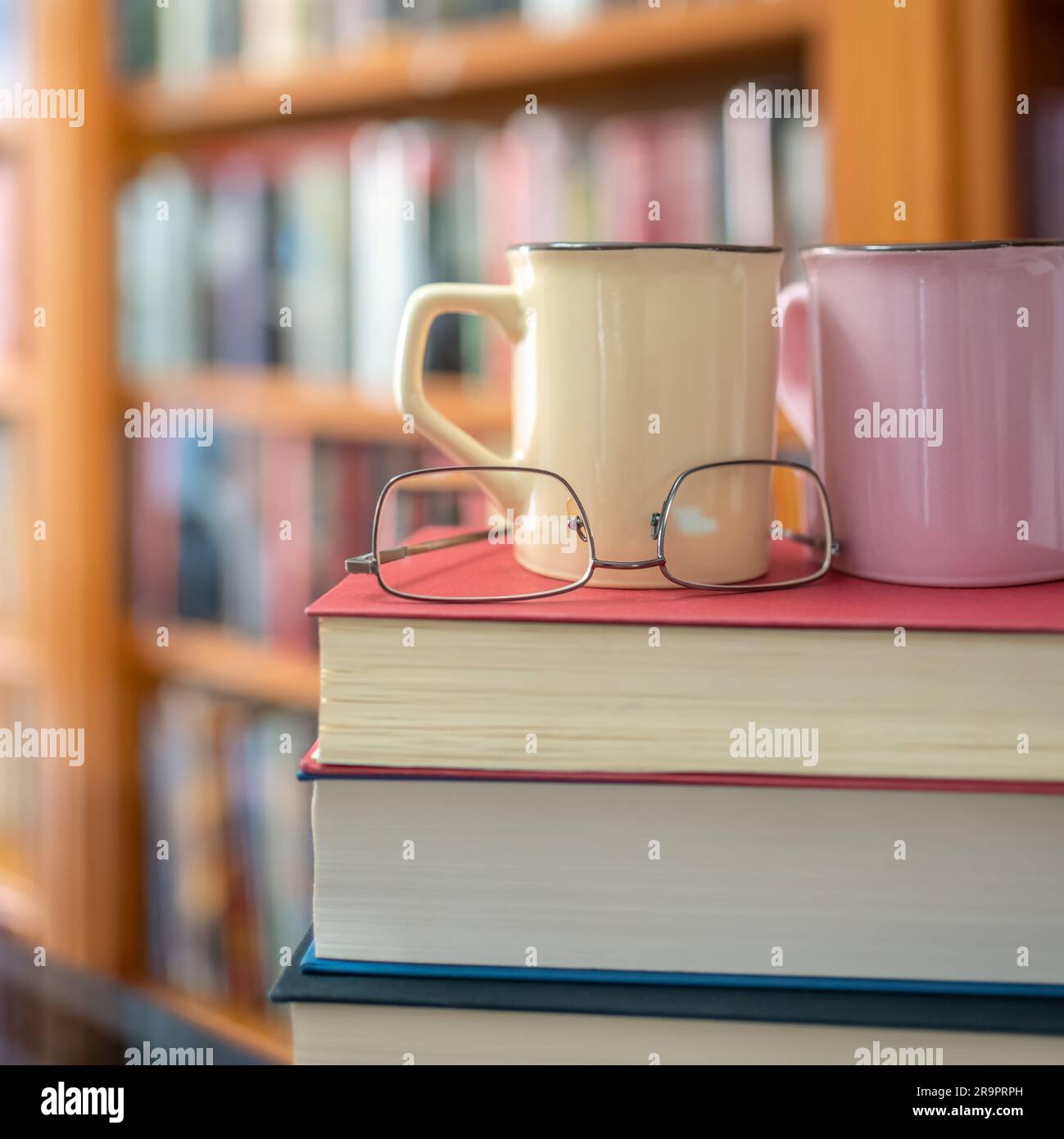 Coffee cups and reading glasses on a stack of books with a bookcase in ...