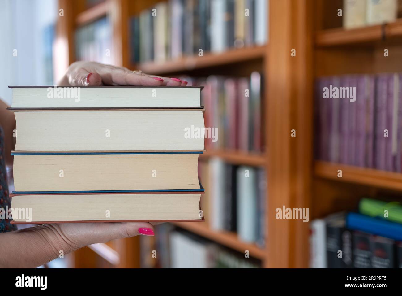 Woman's hands holding a stack of books in front of a bookstore full of ...