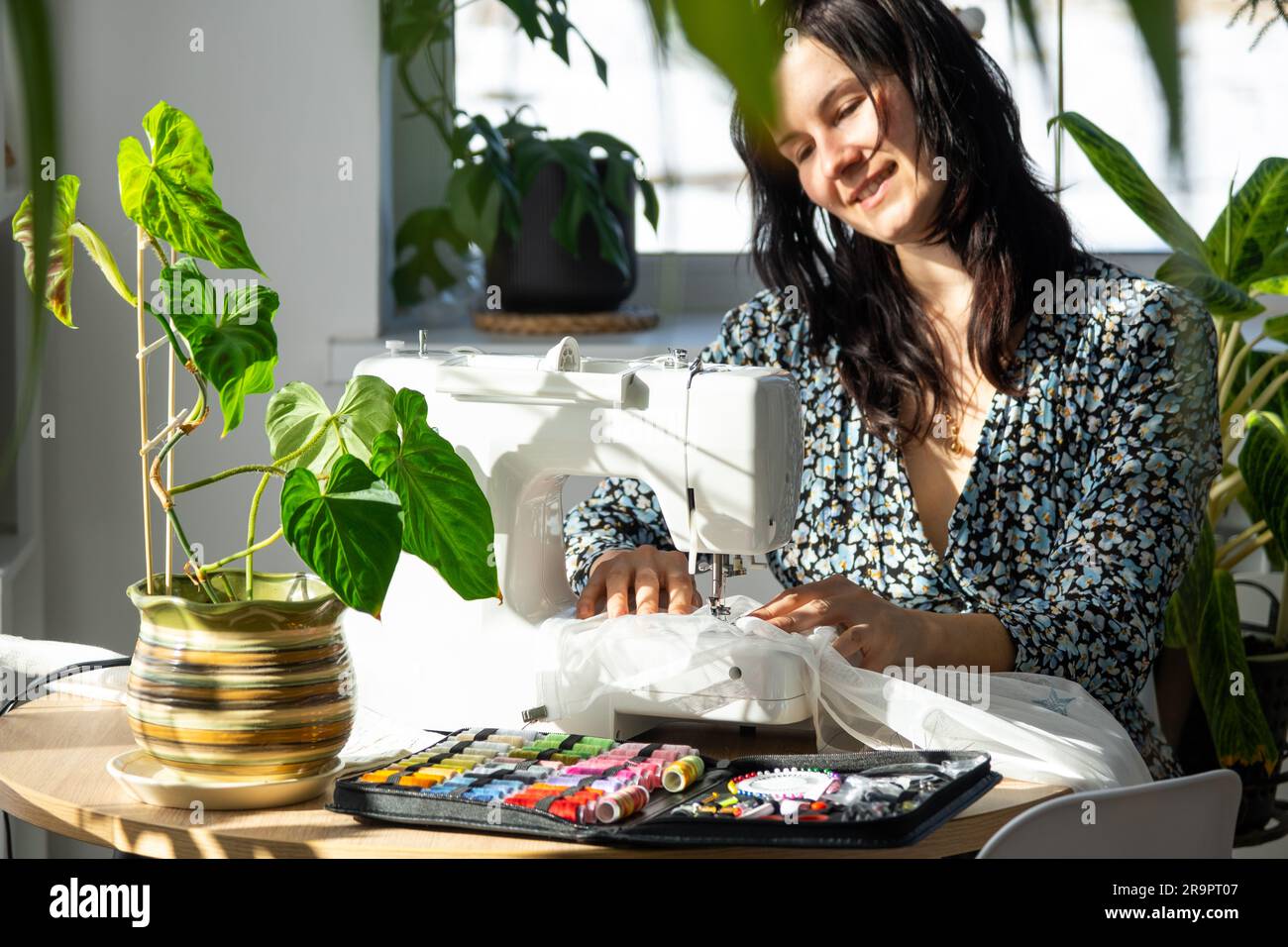 A woman sews tulle on an electric sewing machine in a white modern ...