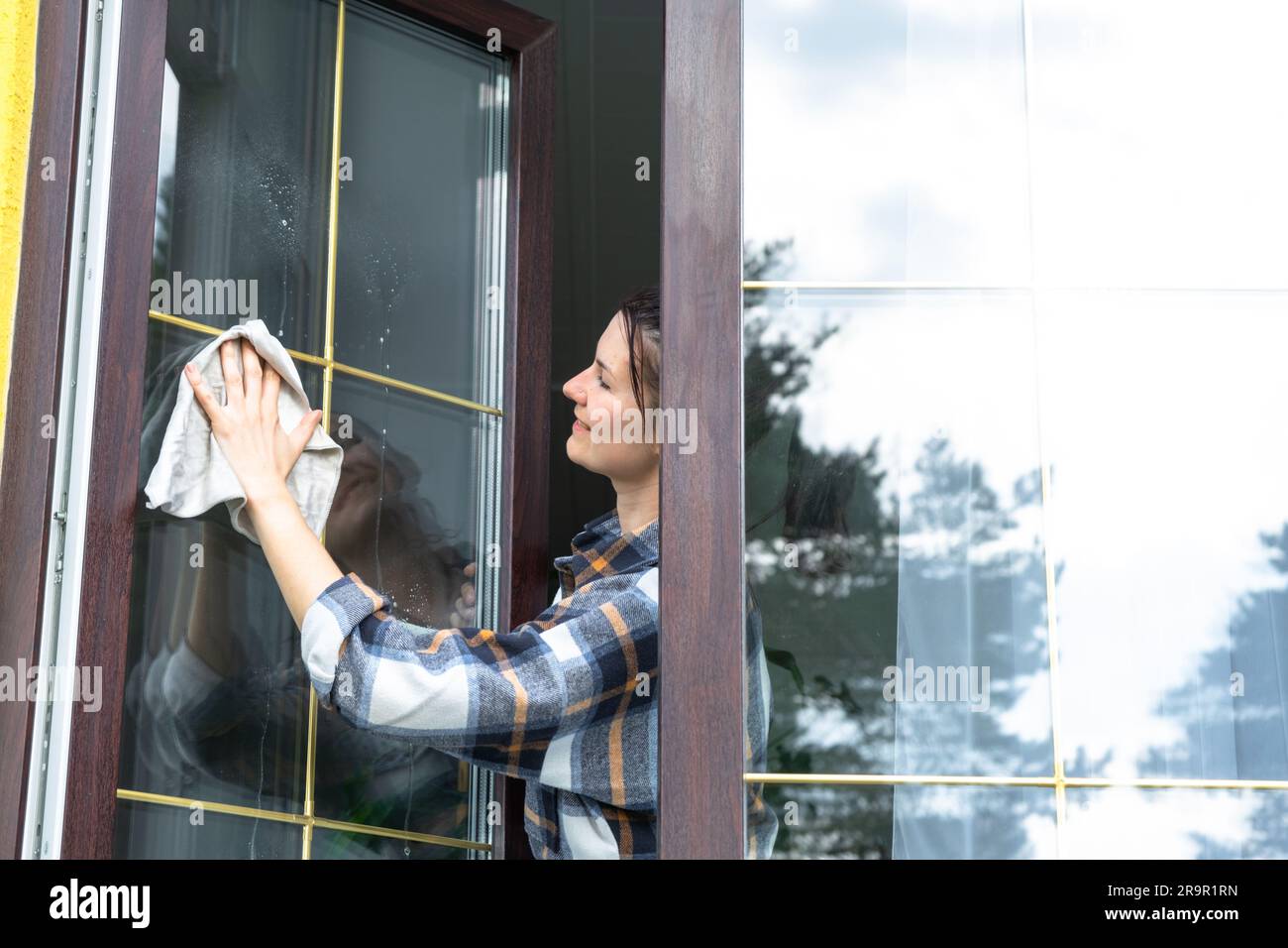 A woman manually washes the window of the house with a rag with a spray ...