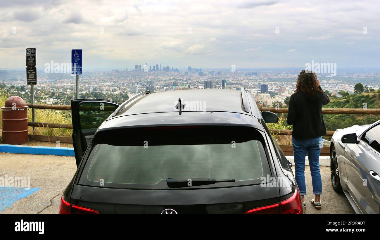 Woman standing next to a car talking on a cellphone at a high overlook ...