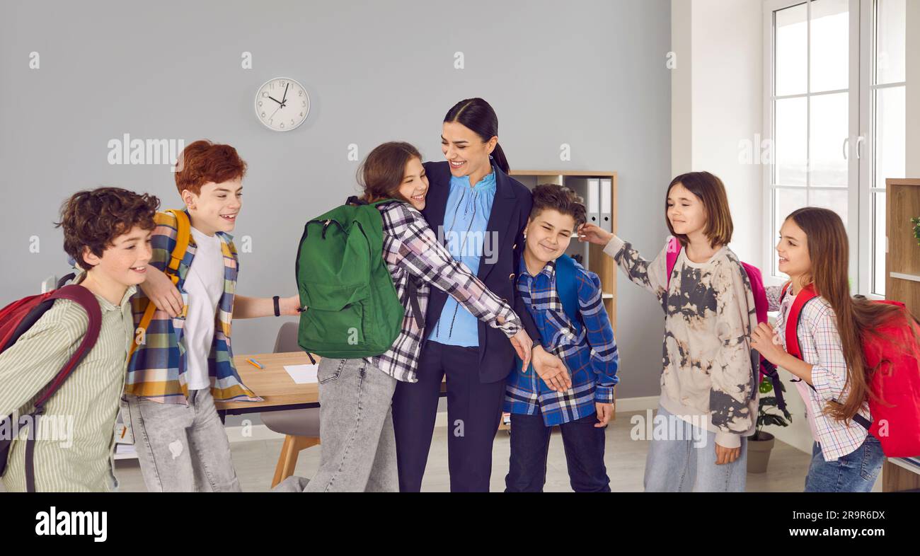 Happy boy and girl students hugging their teacher in classroom Stock ...