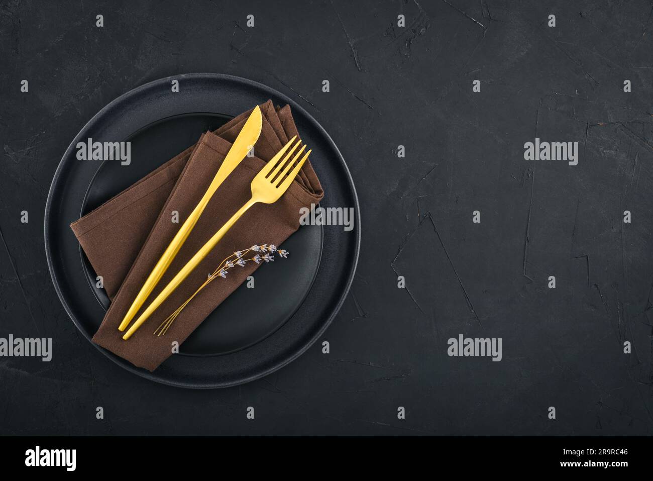Modern minimal table place setting with black plates and golden cutlery ...