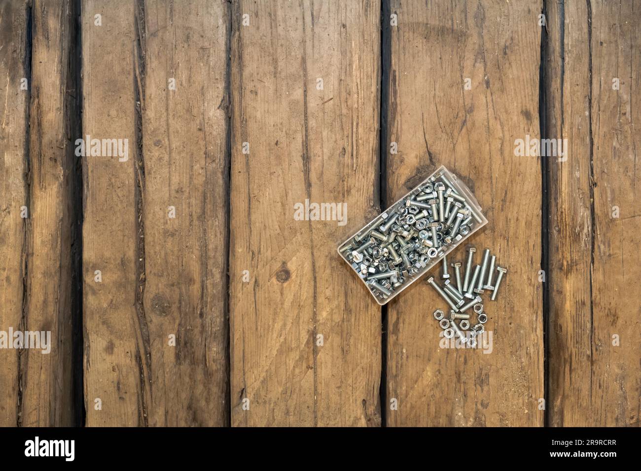 Steel nuts and bolts ina transparent box on the wooden floor. Screws ...