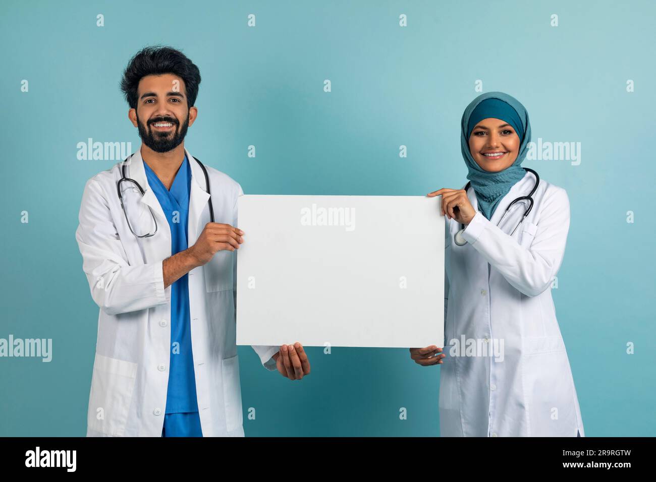 Happy arab doctors in medical uniform and hijab showing blank placard ...