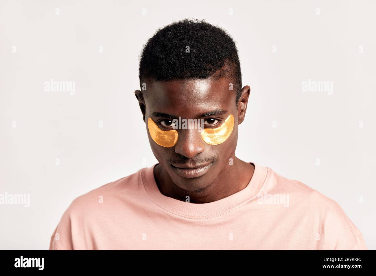 African millennial guy practicing skincare and grooming with under eye ...