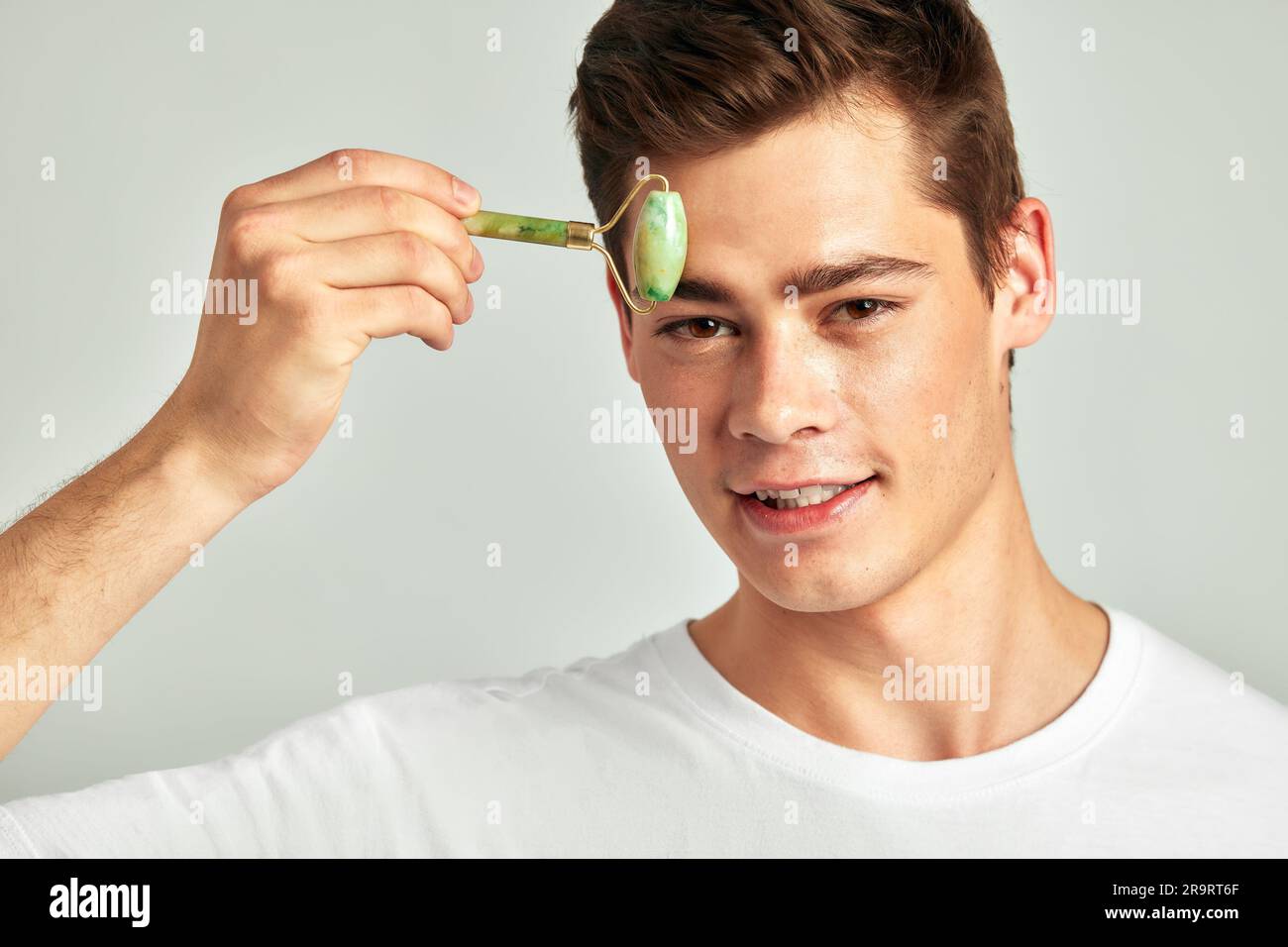 Young handsome smiling guy with brown hair in a white t-shirt using ...