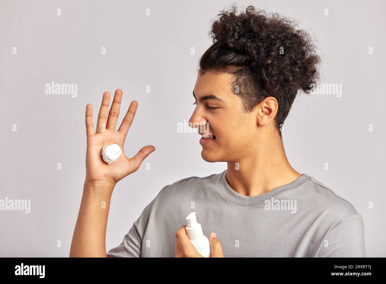 Young handsome smiling guy with black curly hair applying facial mask ...