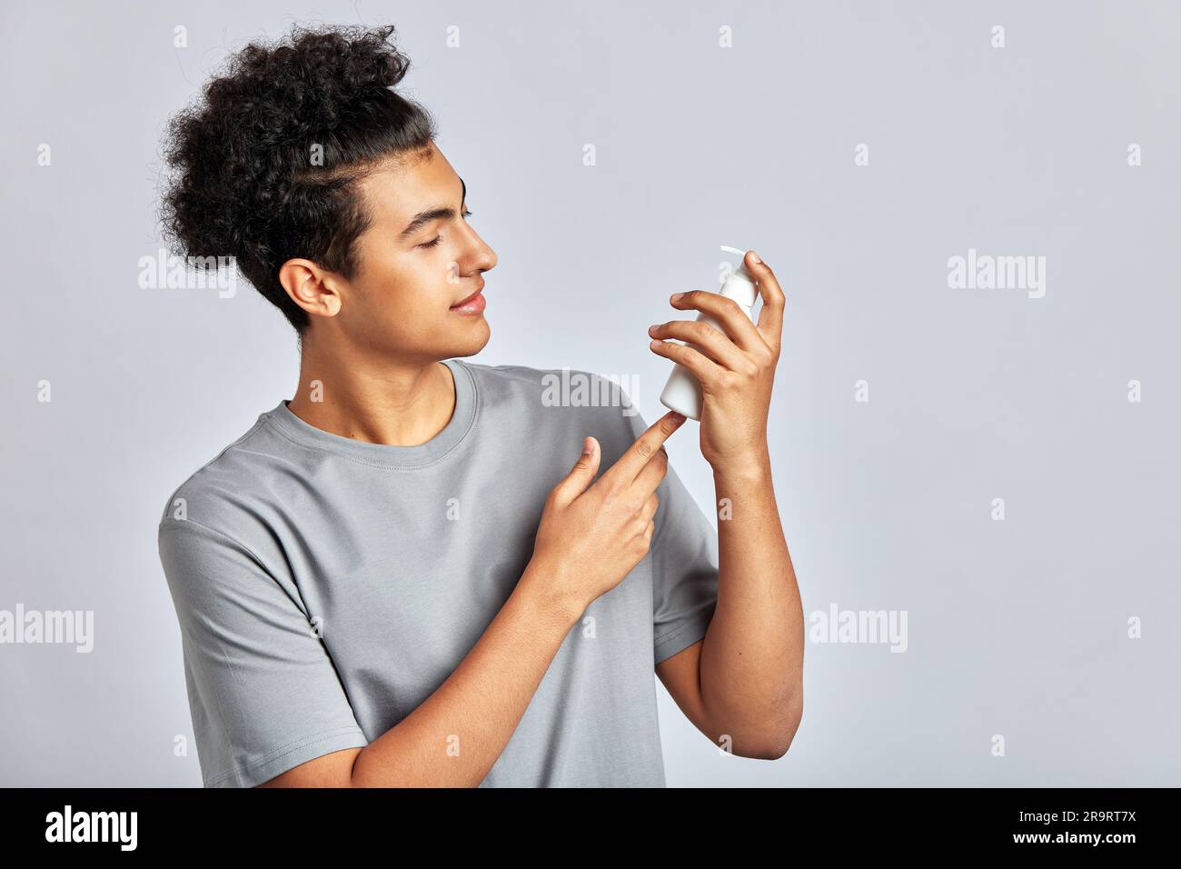 Young handsome smiling guy with black curly hair holding a bottle of ...