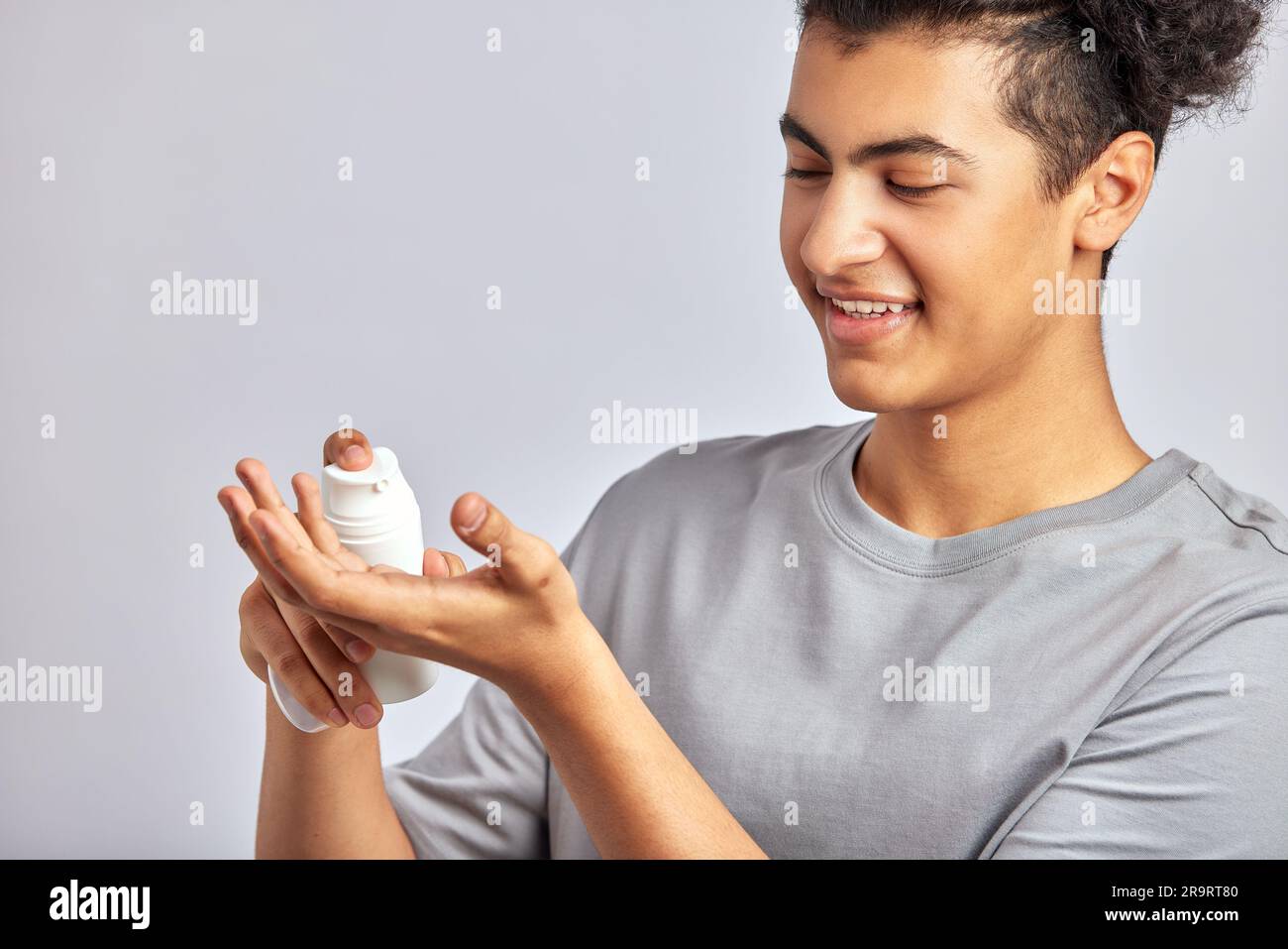 Young handsome smiling guy with black curly hair applying facial mask ...