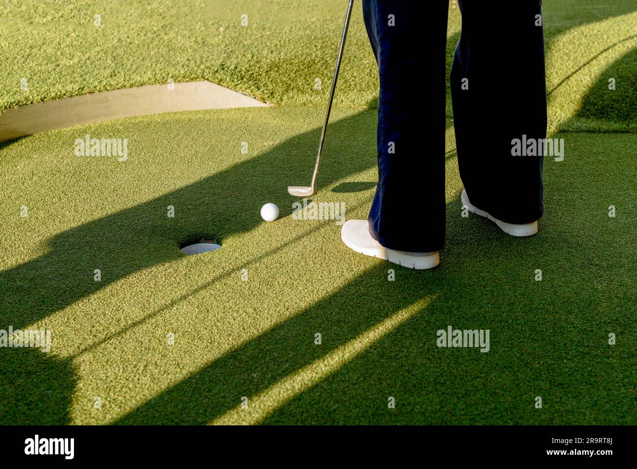 Mini Golf player with grey sneakers putting golf ball into the hole on ...