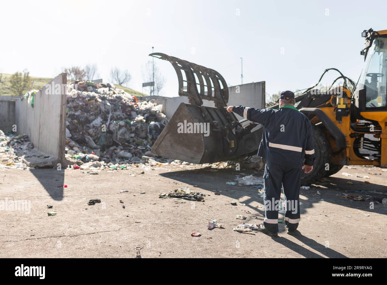 Landfill worker directing skid steer loader on the garbage heap. Waste ...