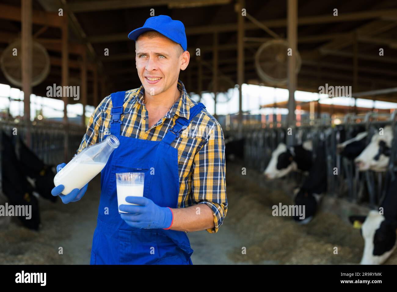Smiling dairy farm owner pouring milk from bottle into glass in outdoor ...