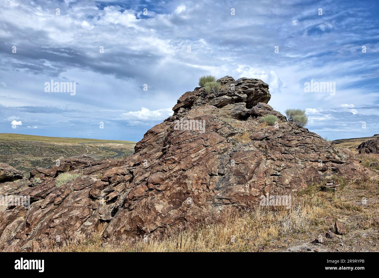 A large rock mound juts out from a hill set against a bright partly ...