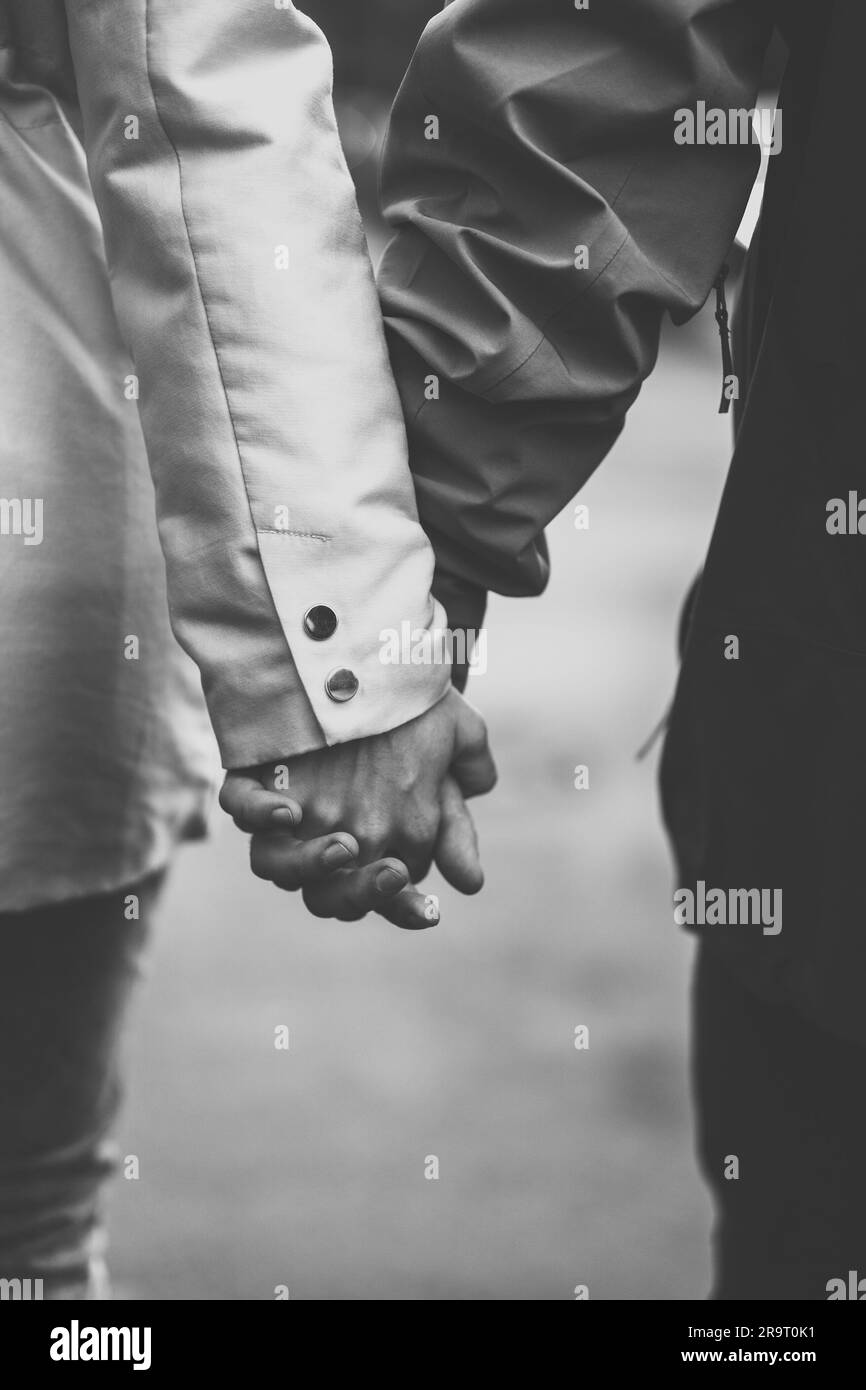 A close-up of two people standing side-by-side, clasping hands in a ...