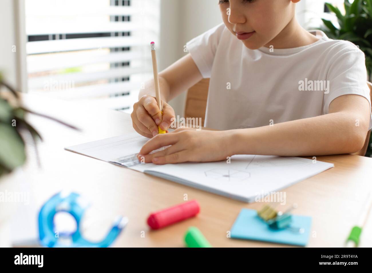A cute boy makes a drawing with a ruler and pencil. Home lessons ...